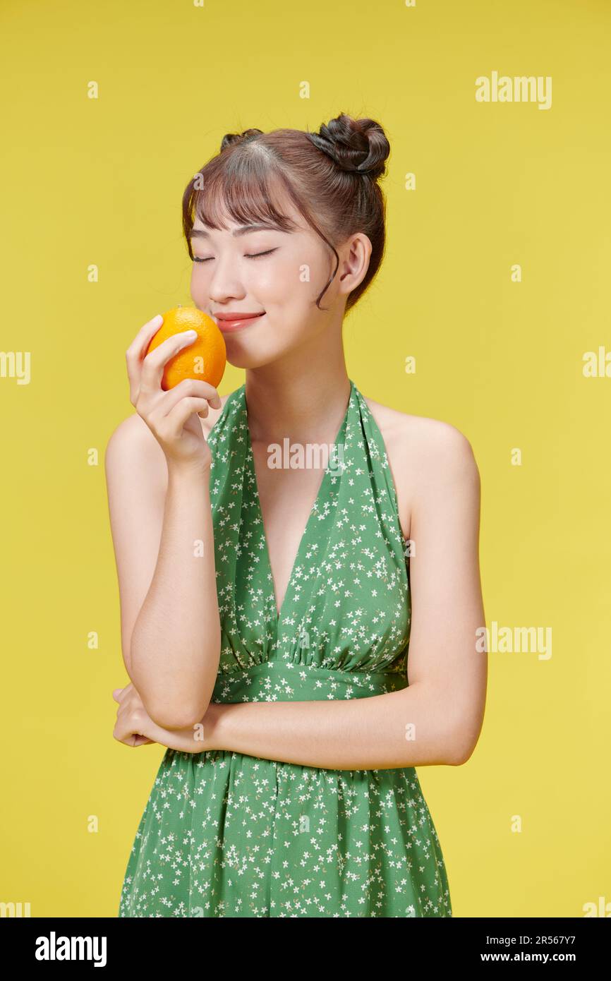 happy young woman smelling an orange fruit over vivid yellow background ...