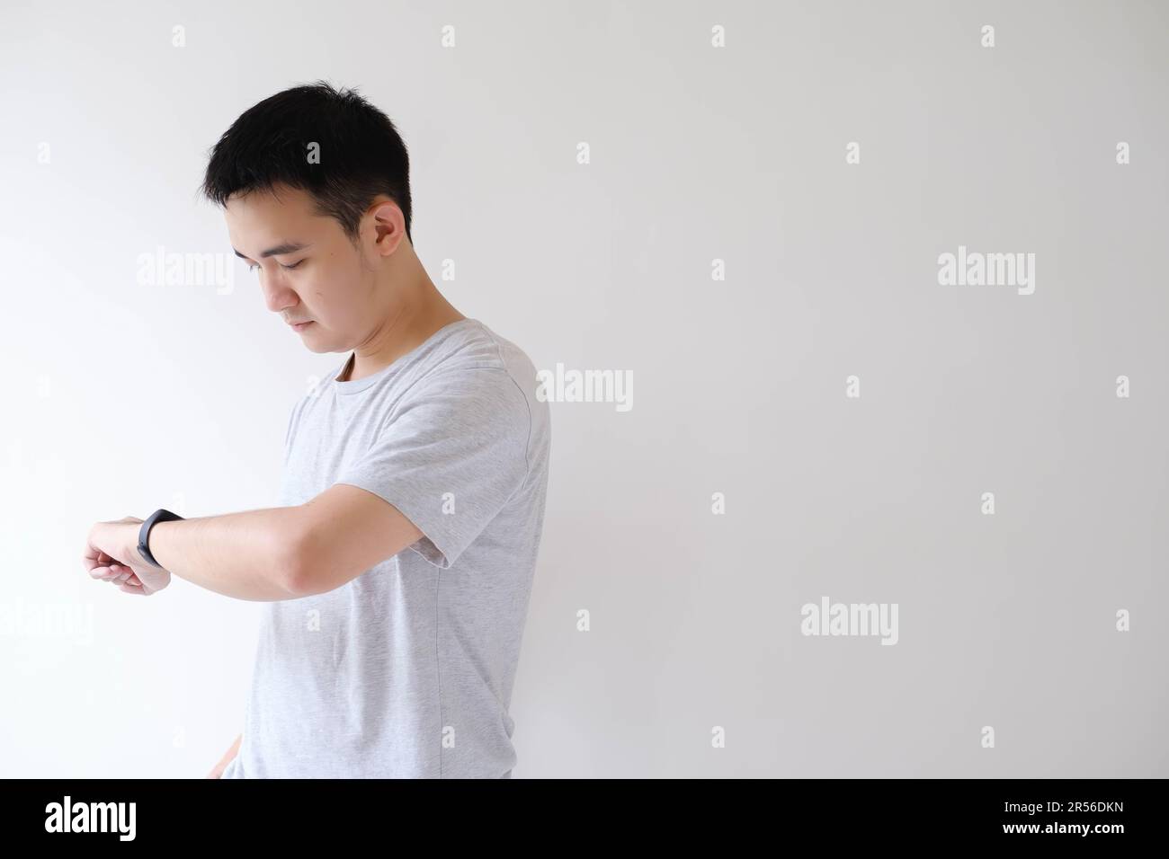 A young Asian man wearing a grey T-shirt is checking the clock on a ...