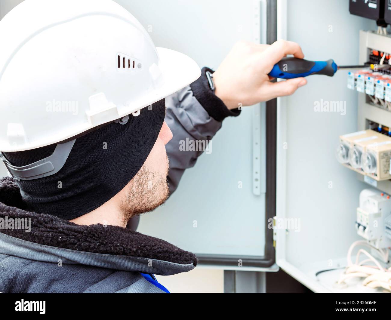Professional electrician in hard hat connects wires with screwdriver in ...