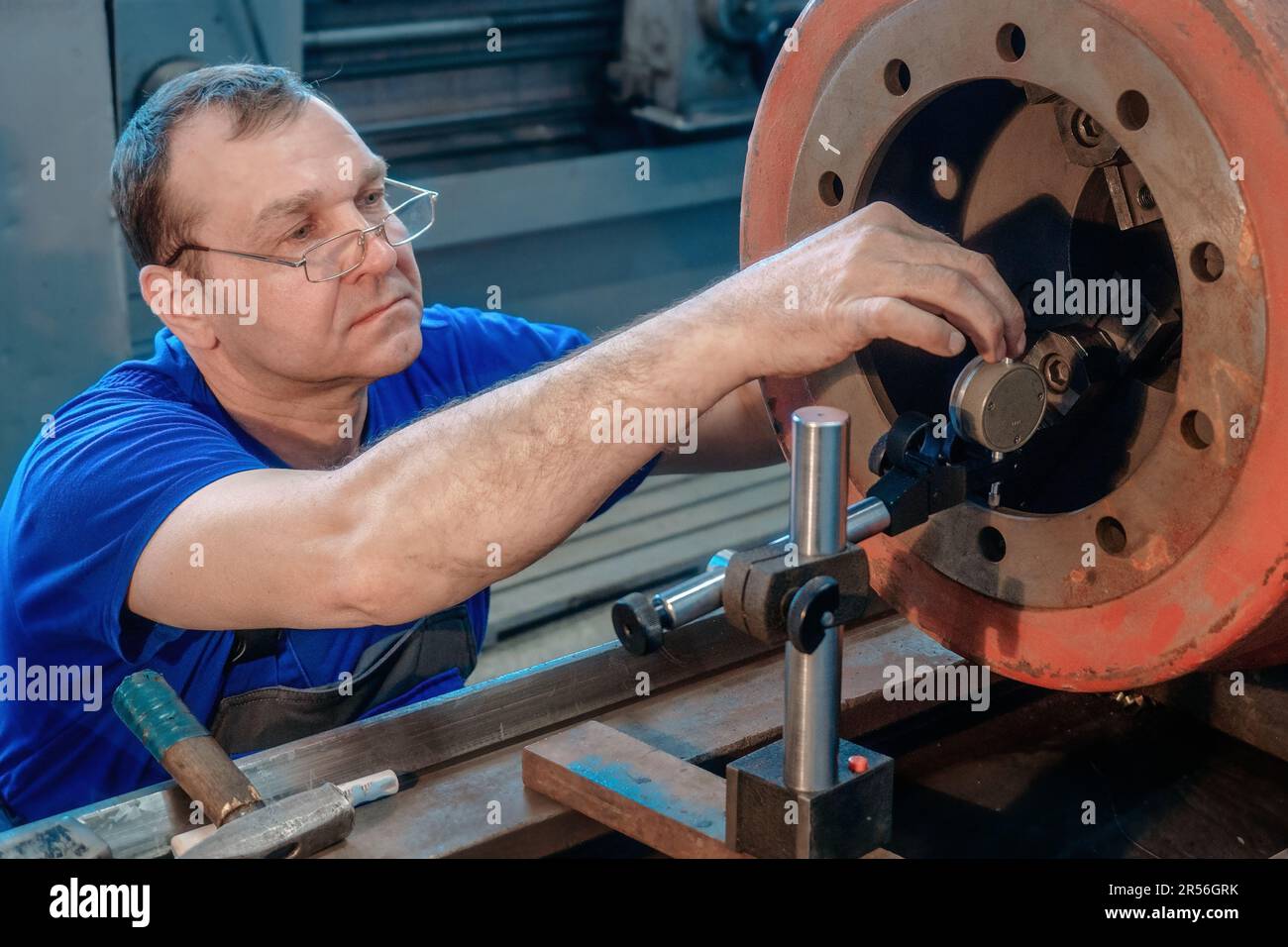 Elderly man with glasses is repairing truck brake disc in lathe workshop. Professional turner at ...