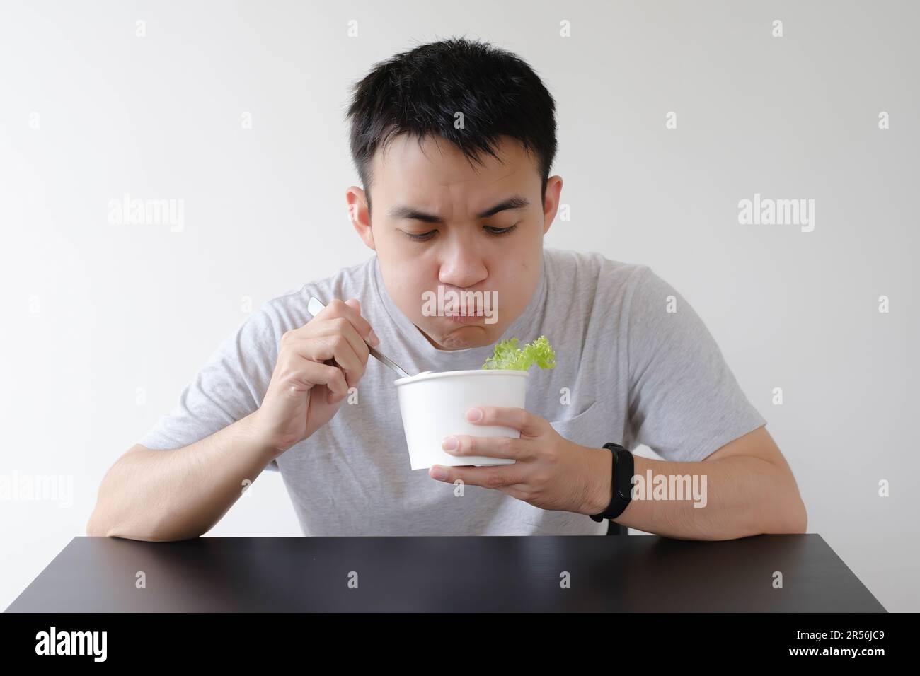 A young Asian man wearing a grey t-shirt and a smartwatch on his left ...
