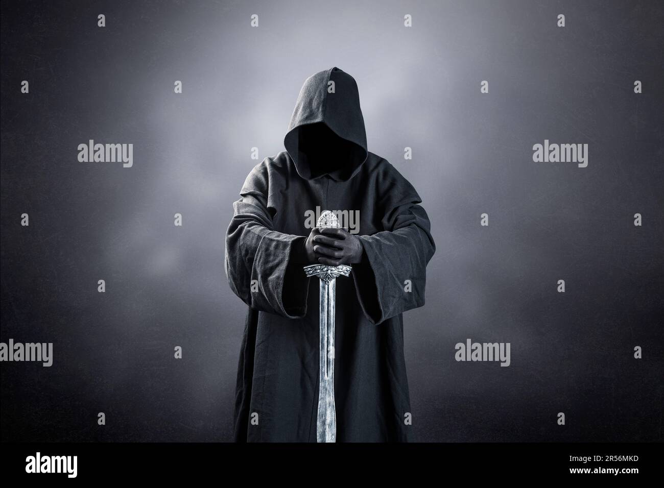 Warrior with hooded cape and medieval sword over dark misty background ...