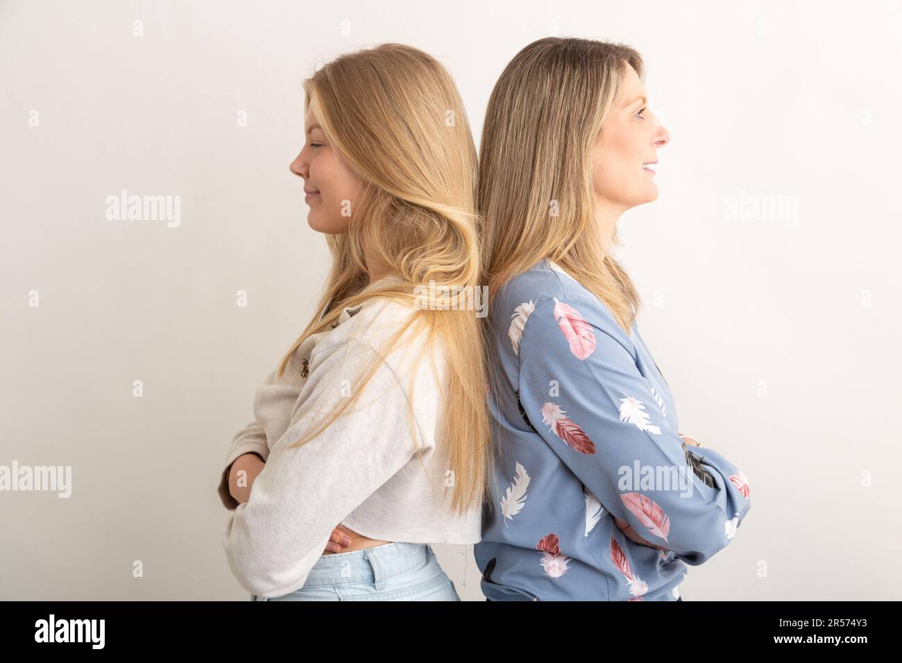 A Mother And Her Adult Daughter Standing Back To Back With Arms Crossed
