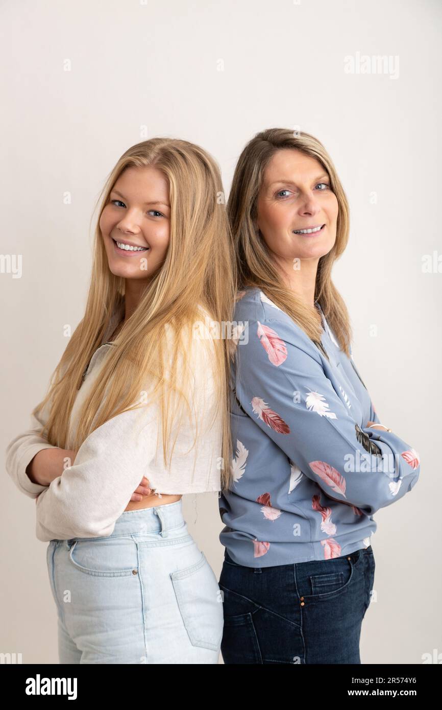 A Mother And Her Adult Daughter Standing Back To Back With Arms Crossed