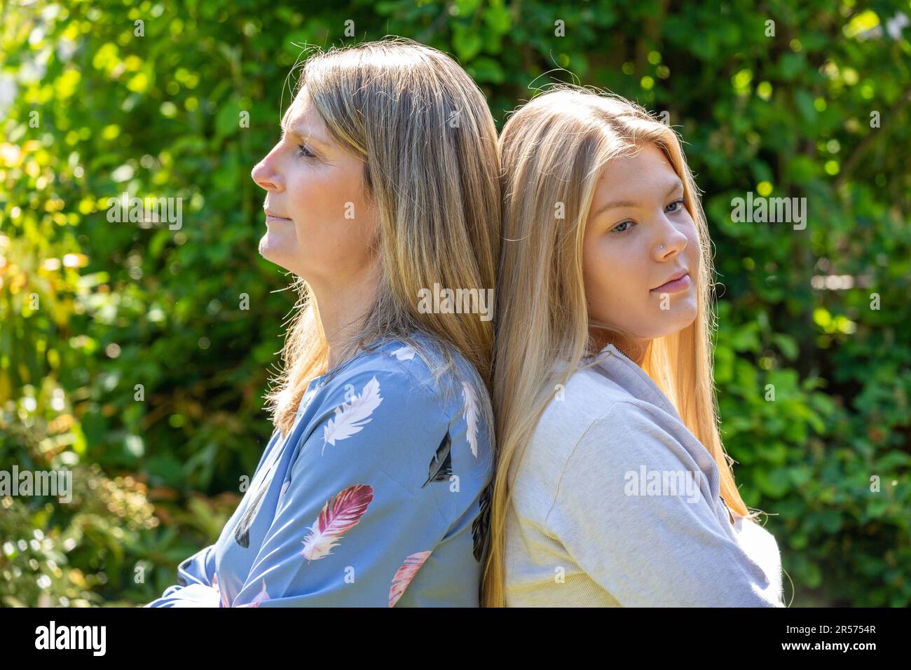 Mother & adult daughter standing back to back outside Stock Photo - Alamy