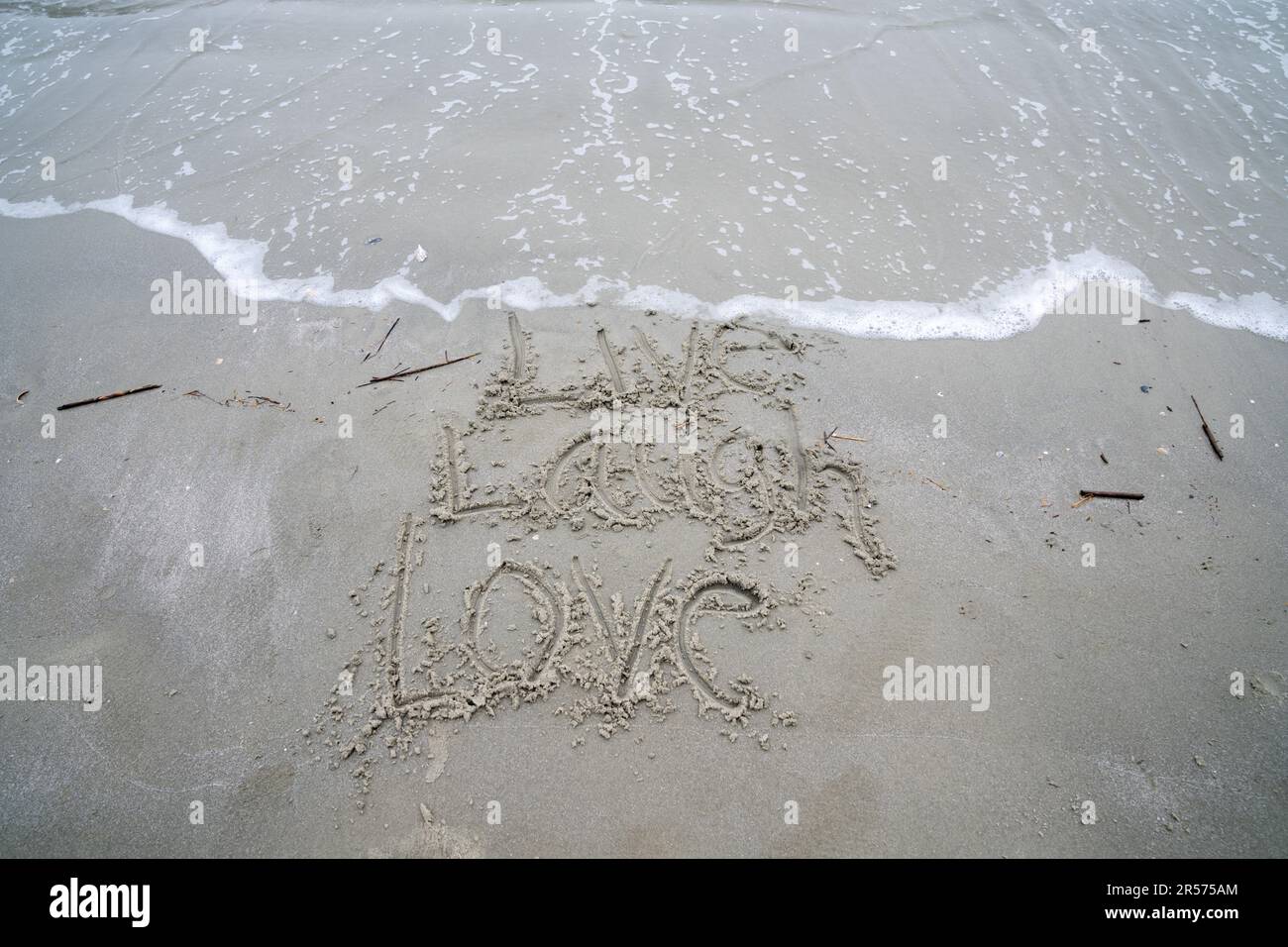 Live Laugh Love phrase written on the beach in the sand as the ocean ...