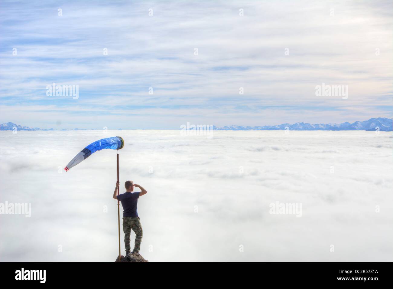 A man with a tall weather vane looks from above at the snowless clouds ...