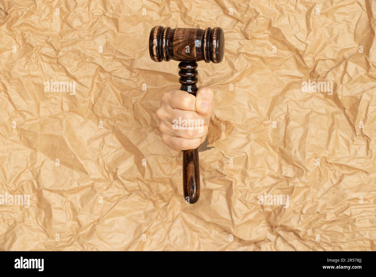 Judge's gavel in girl's hand sticks out of torn brown crumpled paper ...