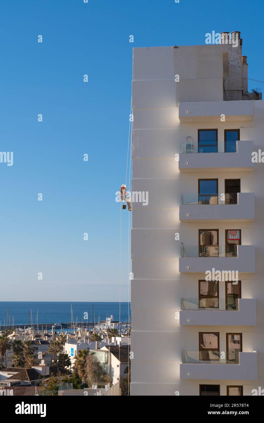 Worker doing high painting work on the side of a building at height on ...