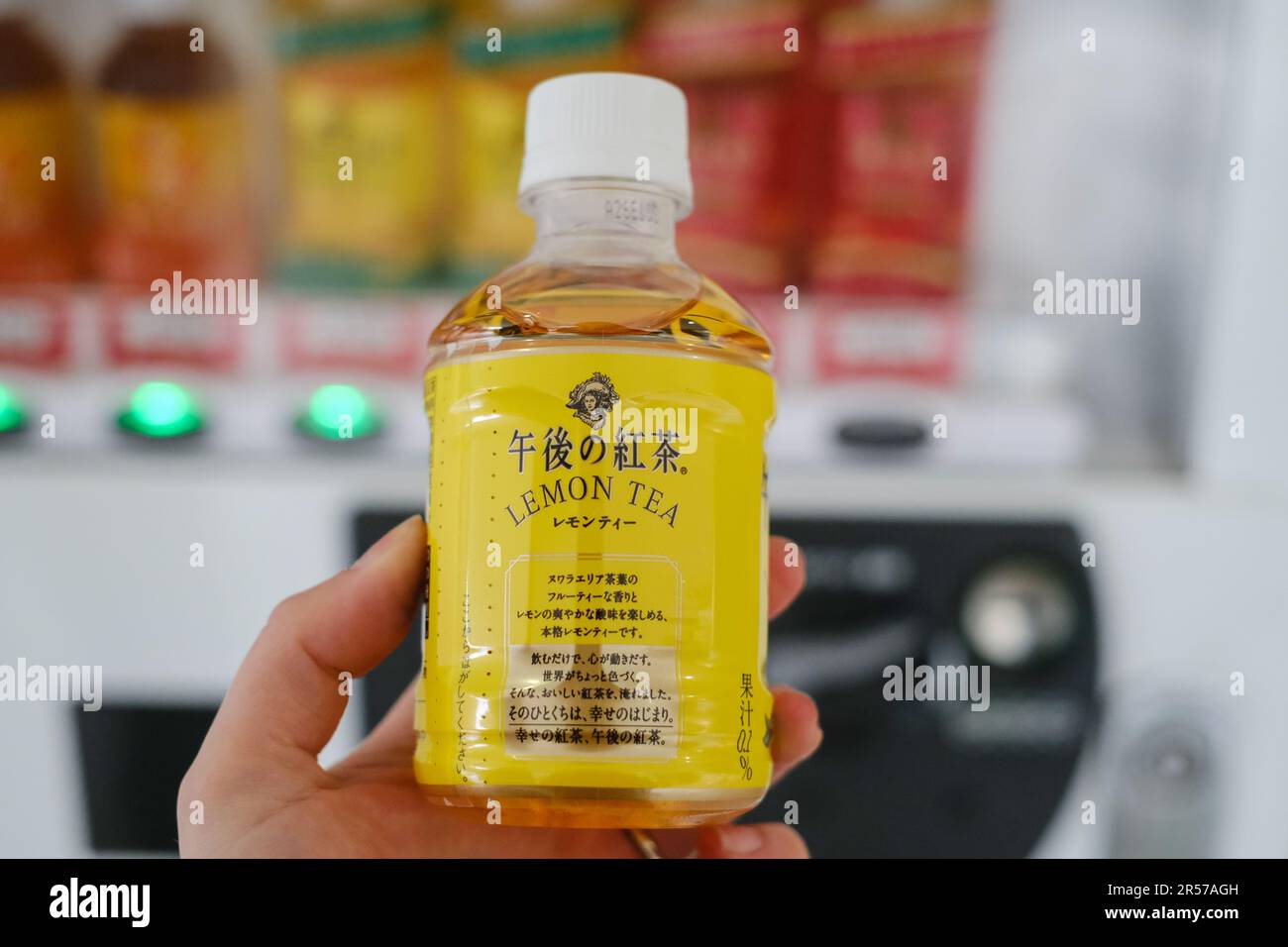A bottle of lemon tea being held in front of a vending machine, Japan ...