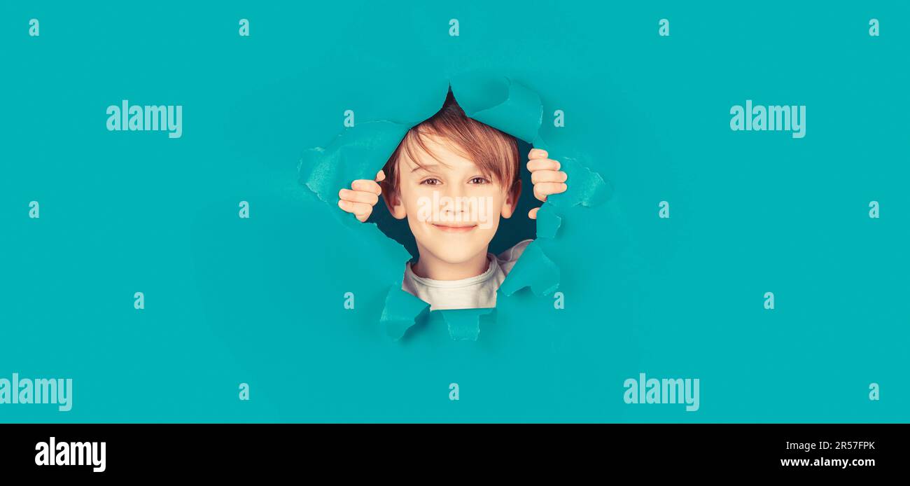 . Kid with toothy smile shows face in paper hole. Positive child with ...