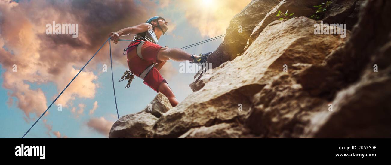 Muscular climber man in protective helmet abseiling from cliff rock ...