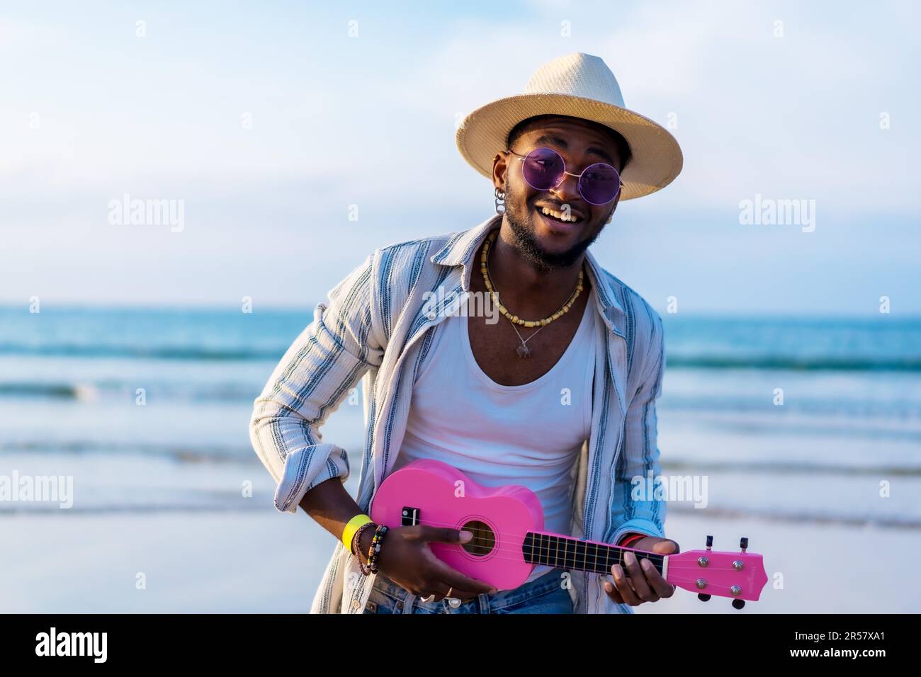 Black ethnic man playing ukulele by the sea enjoying summer vacation on ...