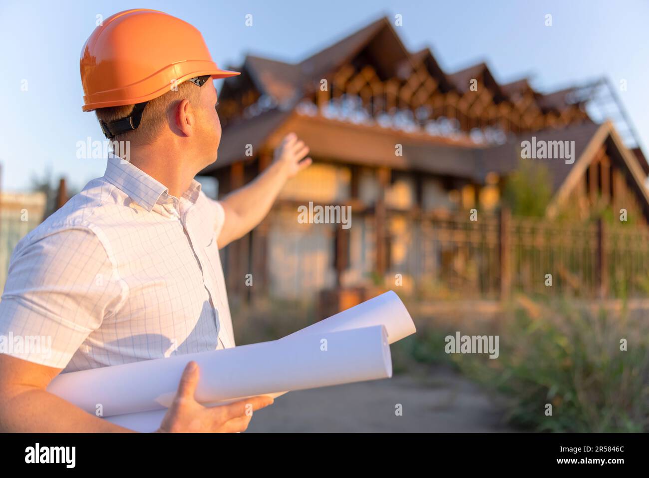 Young engineer in a yellow helmet with blueprints at a construction ...