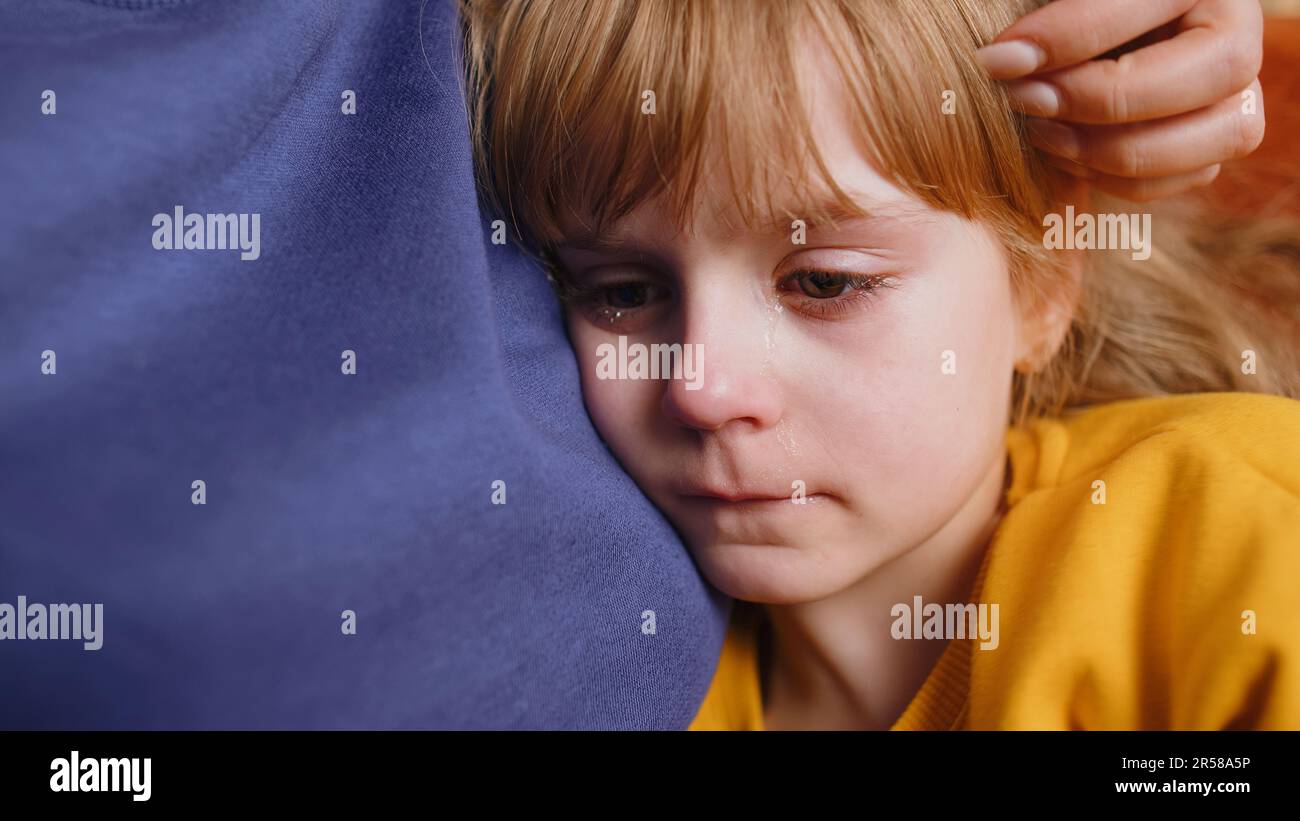 Close-up of sad girl kid is crying and lying on mother at home ...