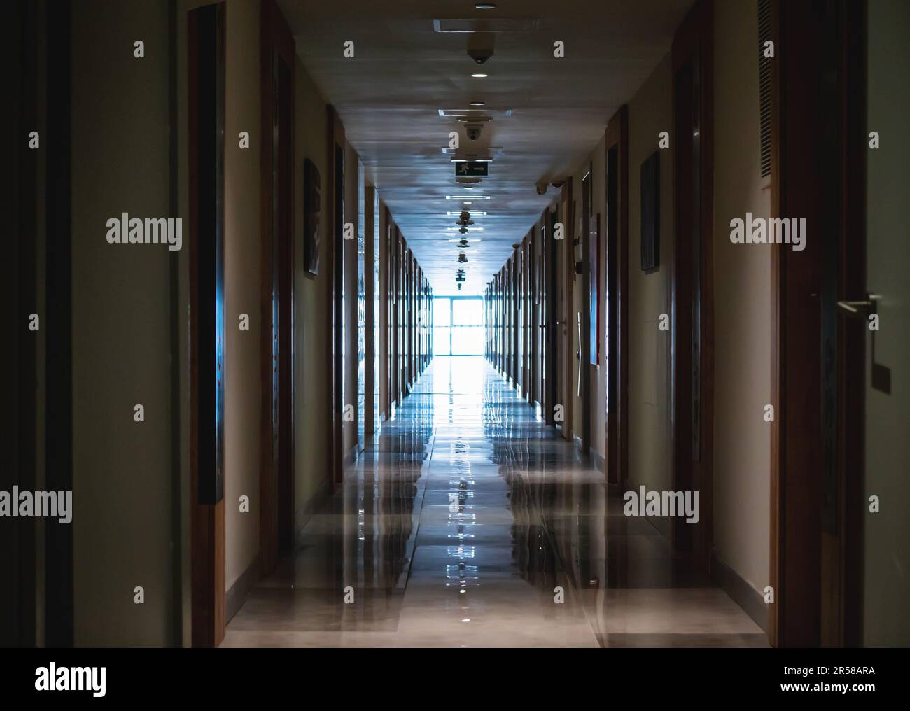 Dark long corridor in hotel with many doors and light in end from big ...