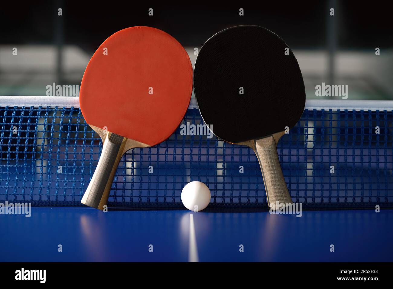 Pair of racket and ball on tennis table against grid net in sport hall ...
