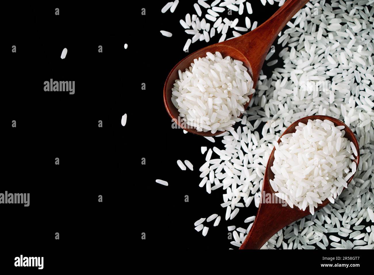 White uncooked rice in wooden spoons on black background. Raw grains of ...