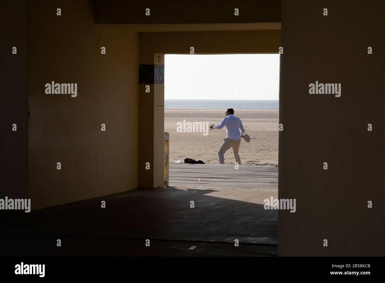 Man playing handball on the beach seen through a door of the Art Deco ...