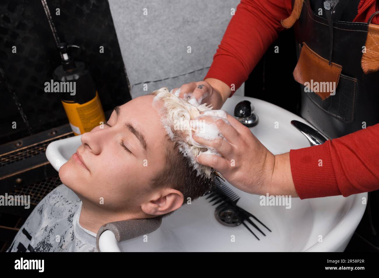 The hands of a professional barber lathered with foam the hair of a ...