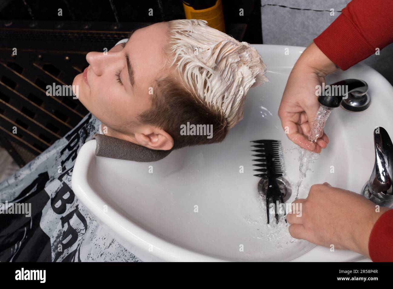 A barbershop client, a young guy with a painted head in white, washes ...