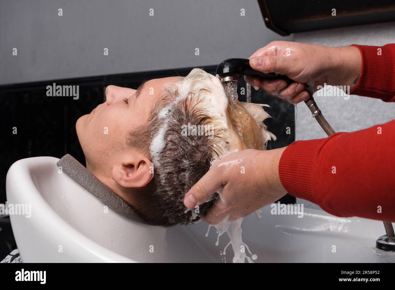 The hands of a professional barber wash the hair and head of a guy's ...