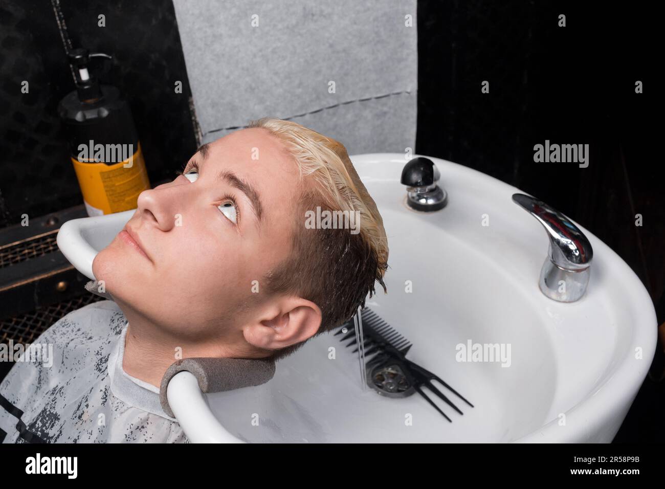 Young handsome guy barbershop customer lying on the sink after washing ...
