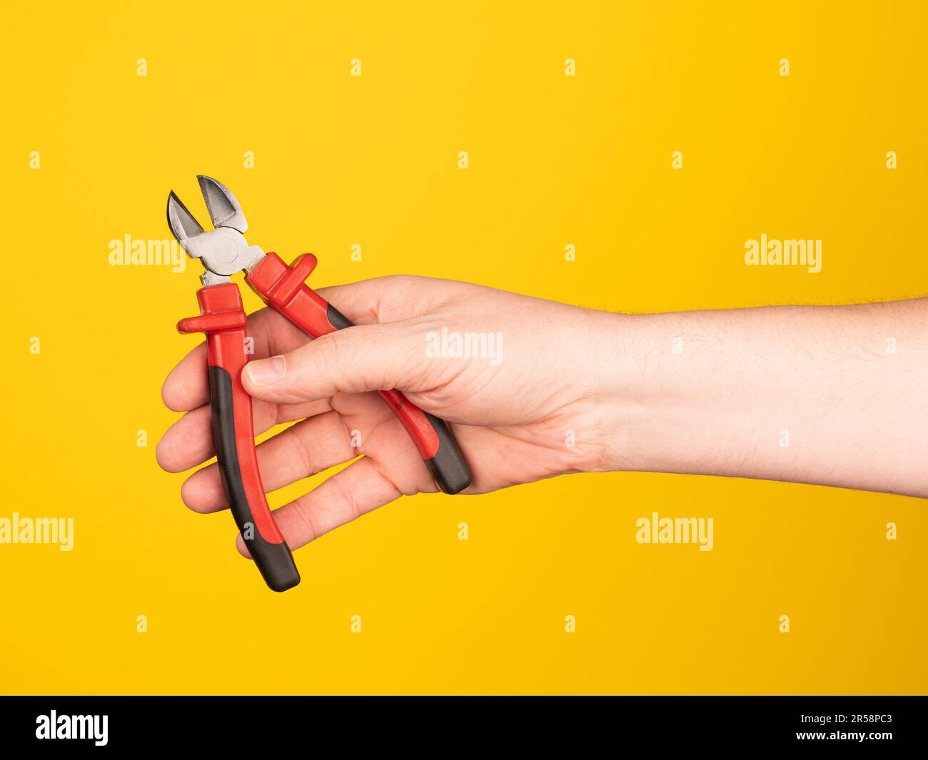 A hand holds a side cutter. No face, yellow background Stock Photo - Alamy