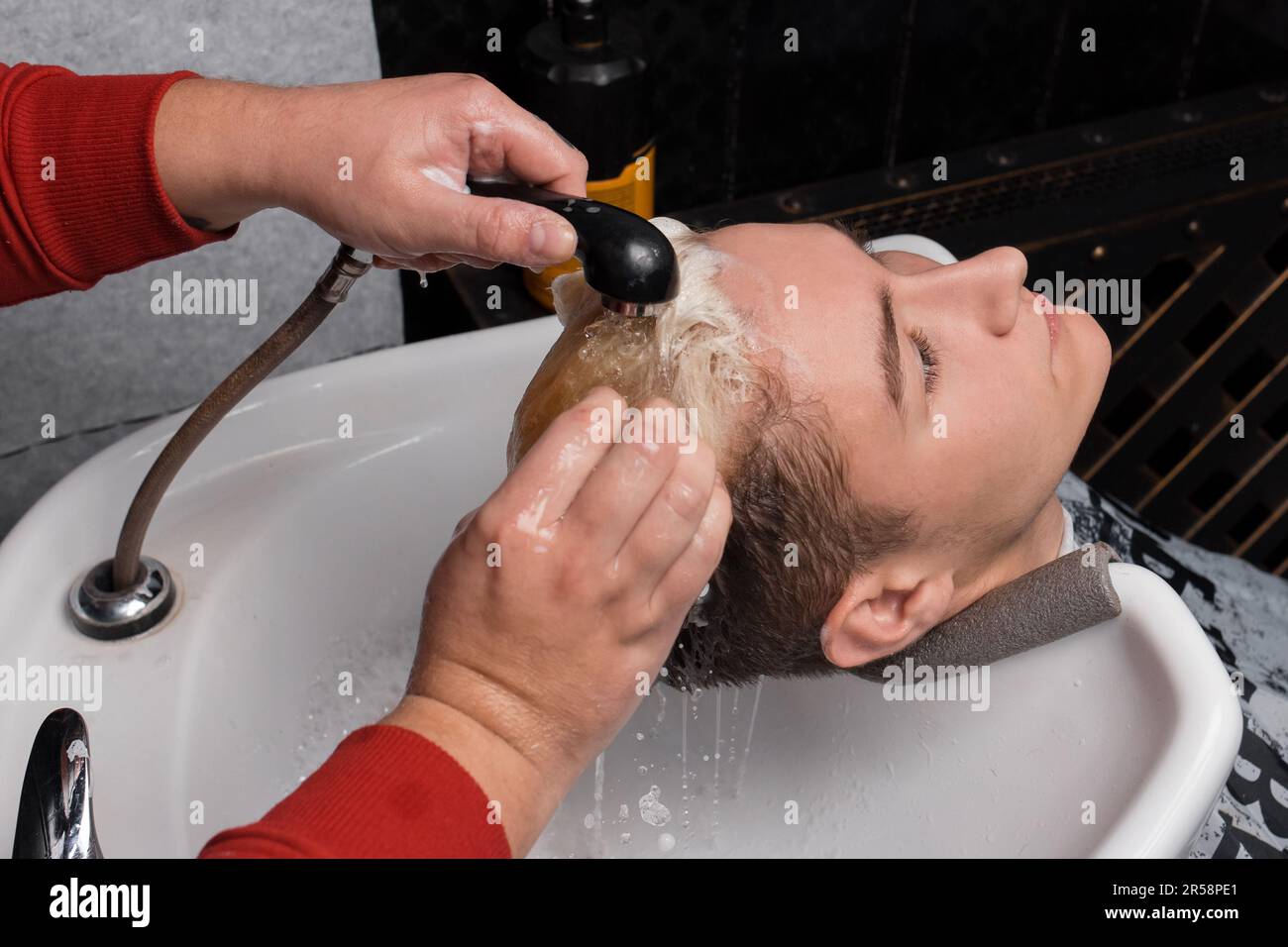 The hands of a hairdresser employee wash the hair and head of a young ...