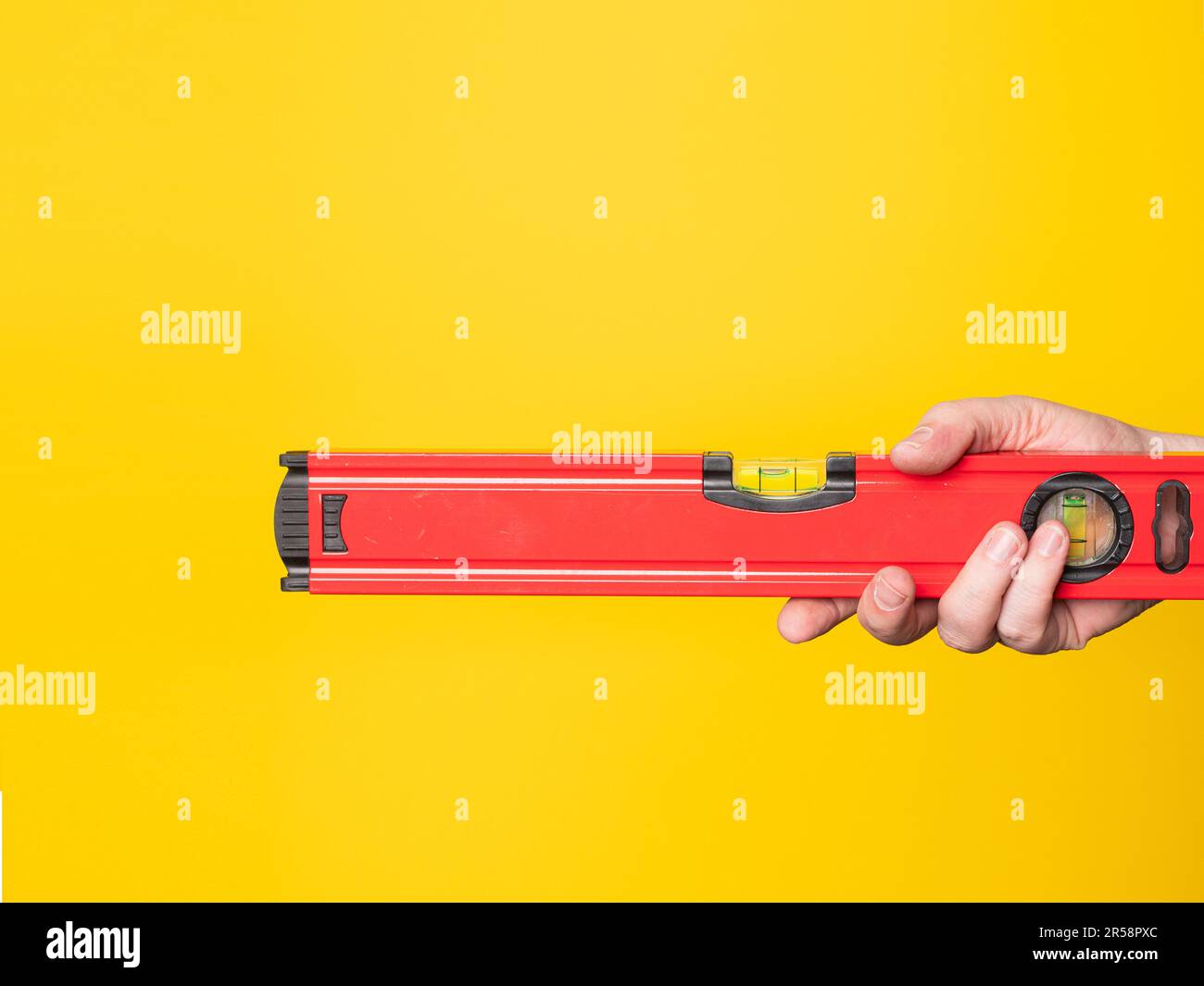 Hand holding a level. Yellow background, no face Stock Photo - Alamy