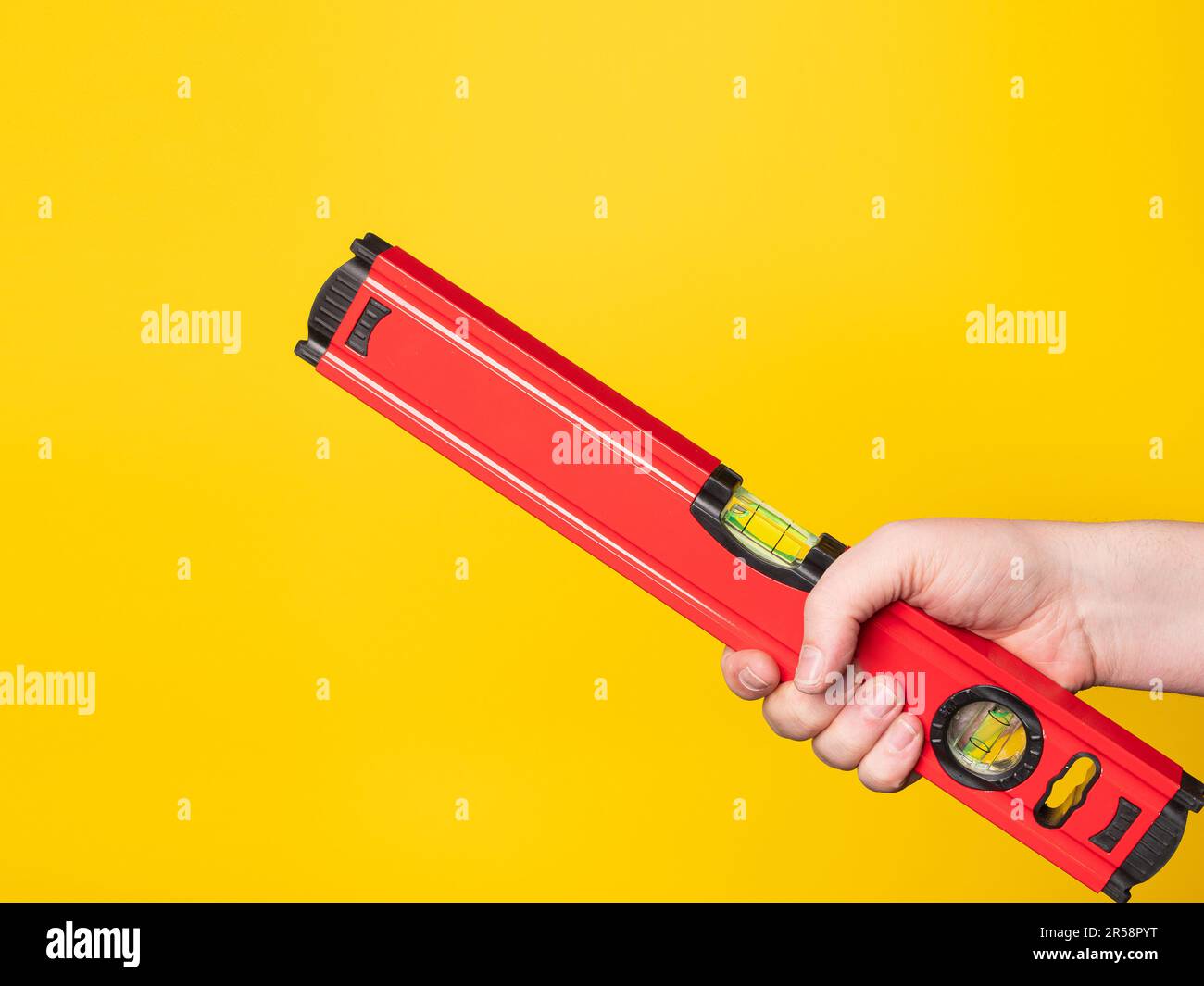 Hand holding a level. Yellow background, no face Stock Photo - Alamy