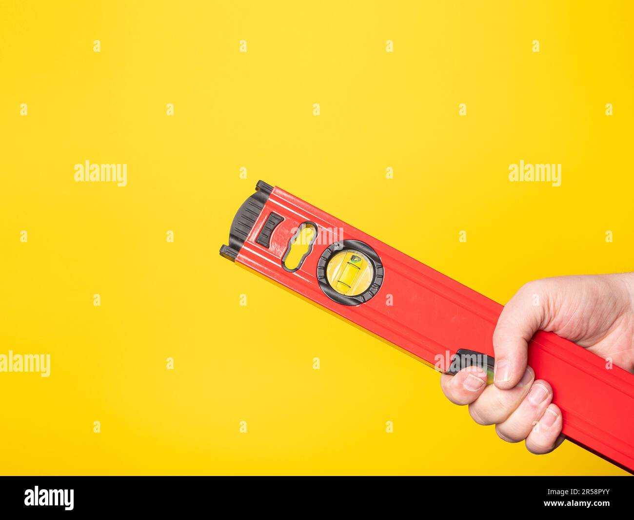 Hand holding a level. Yellow background, no face Stock Photo - Alamy