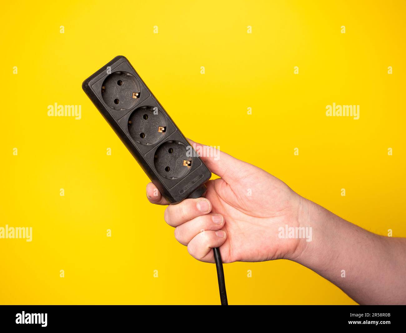 A hand holds a power strip. No face, yellow background Stock Photo - Alamy