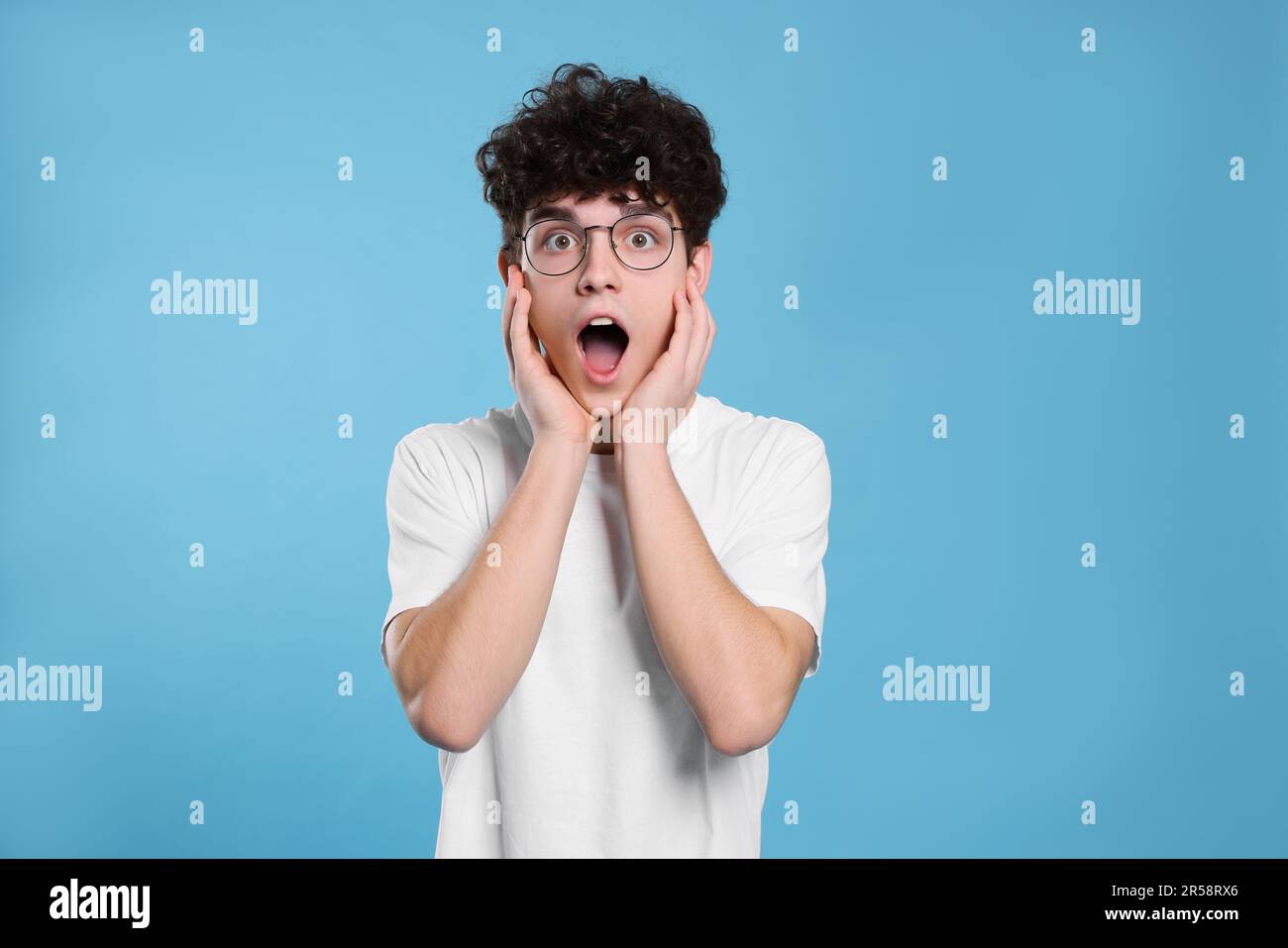 Portrait of shocked teenage boy wearing glasses on light blue ...