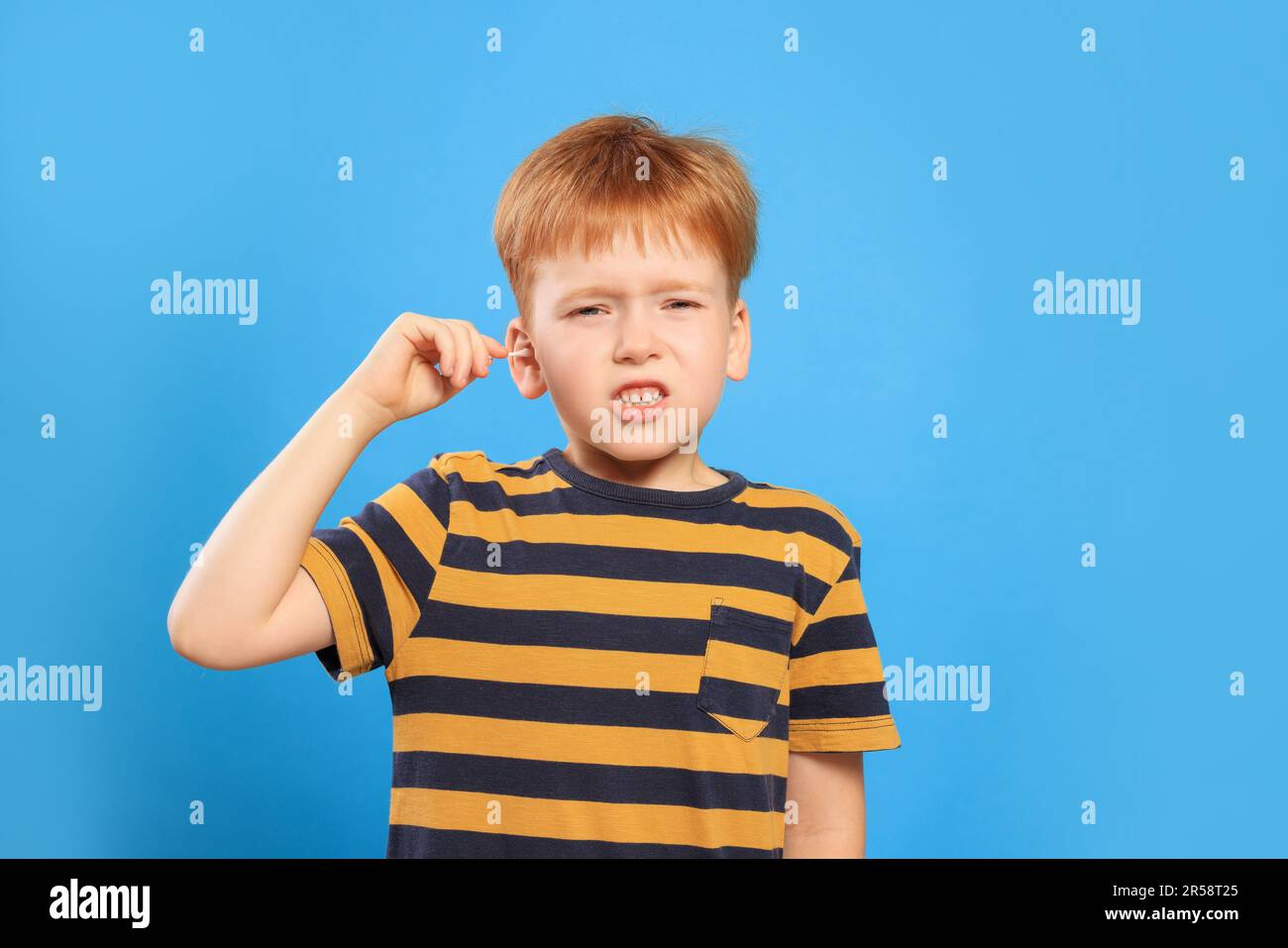 Little boy cleaning ear with cotton swab on light blue background Stock ...