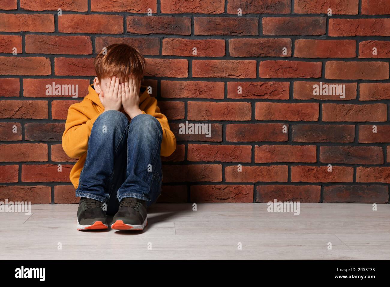 Upset boy sitting on floor near brick wall, space for text. Children's ...