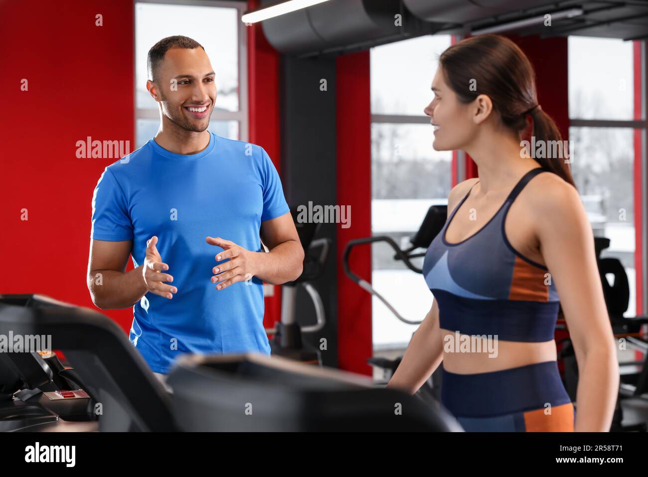 Happy trainer explaining woman how to do exercise properly in modern ...