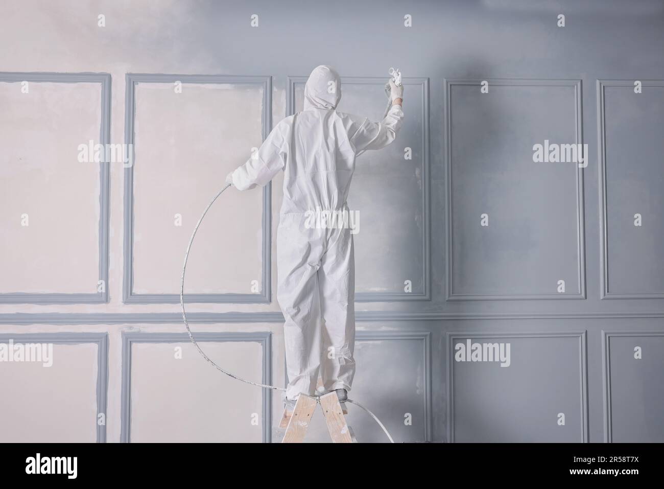 Decorator dyeing wall in grey color with spray paint, back view Stock ...