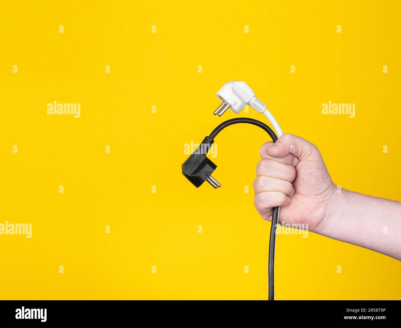 A male hand holds two electric plugs. No face, yellow background, copy ...