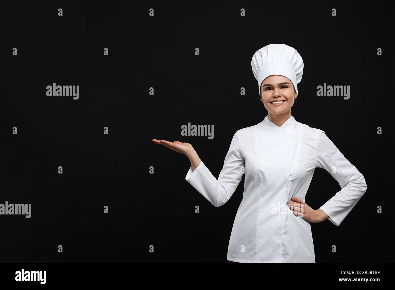 Happy female chef pointing at something on black background. Space for ...