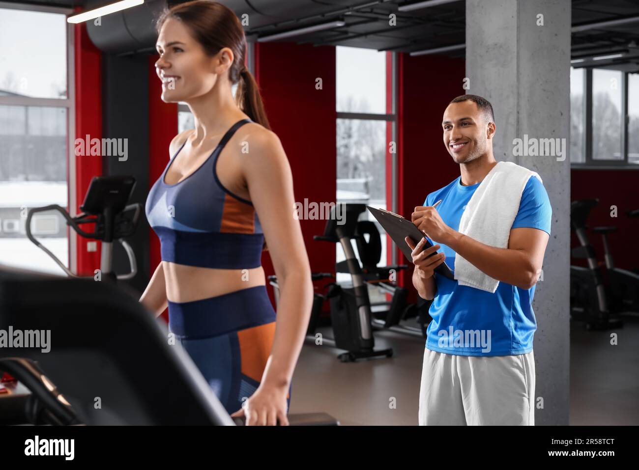 Happy trainer writing down workout plan while woman doing exercise in ...