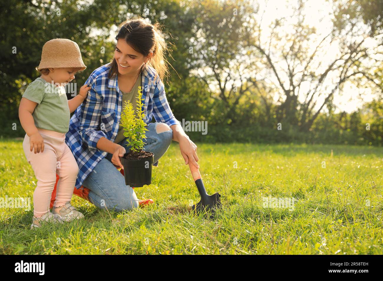 Mother and her baby daughter planting tree together in garden, space ...