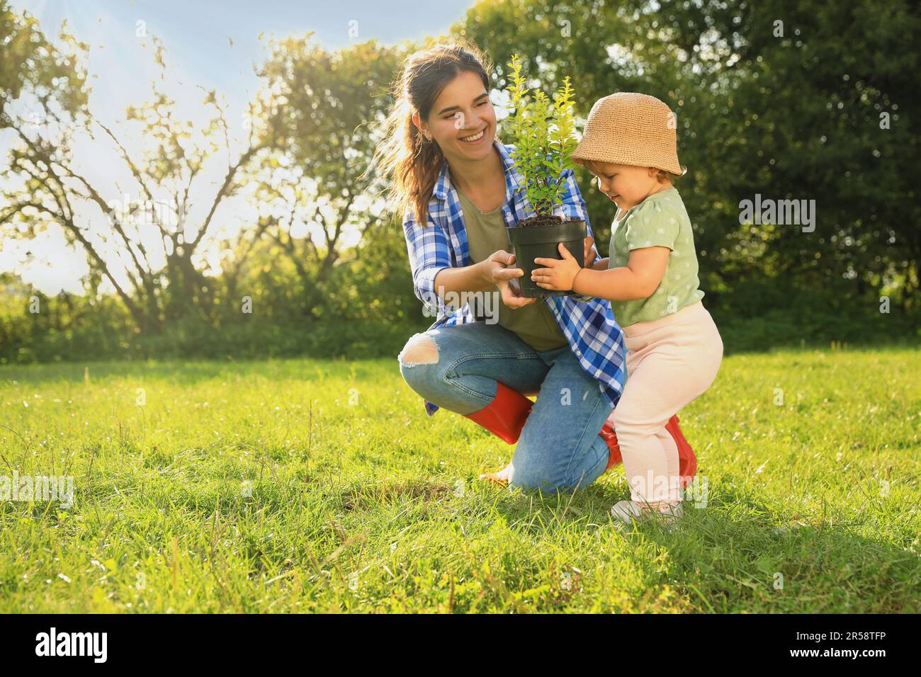 Mother and her baby daughter planting tree together in garden, space ...