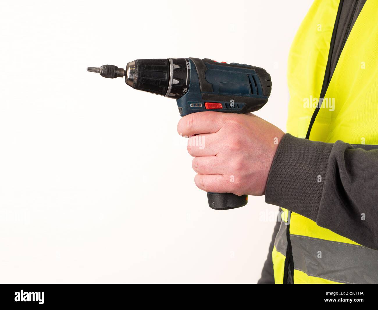 A worker in a safety vest holds a cordless screwdriver in his hand. No ...