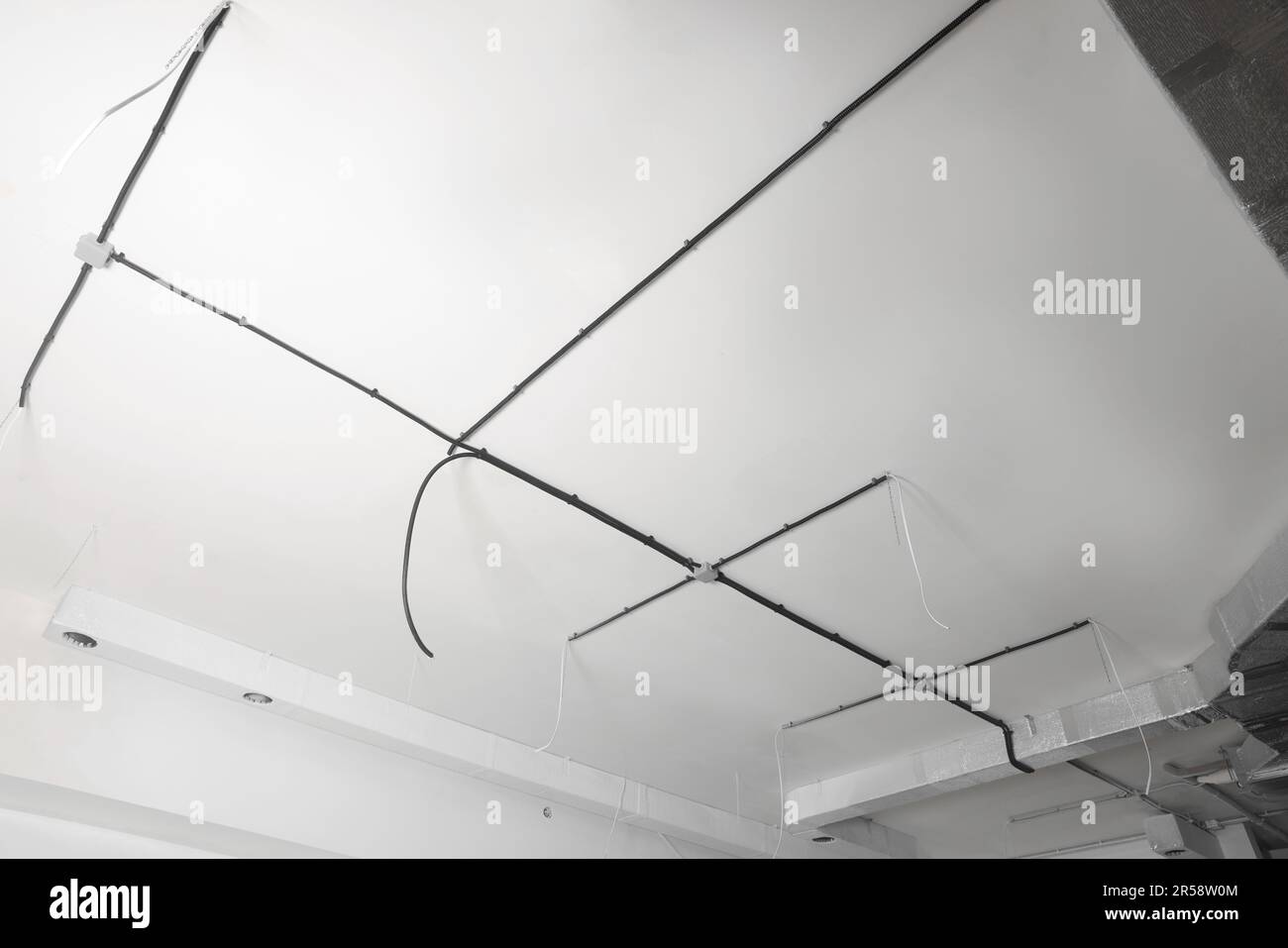 Conduits with cables and ventilation system on white ceiling, low angle ...
