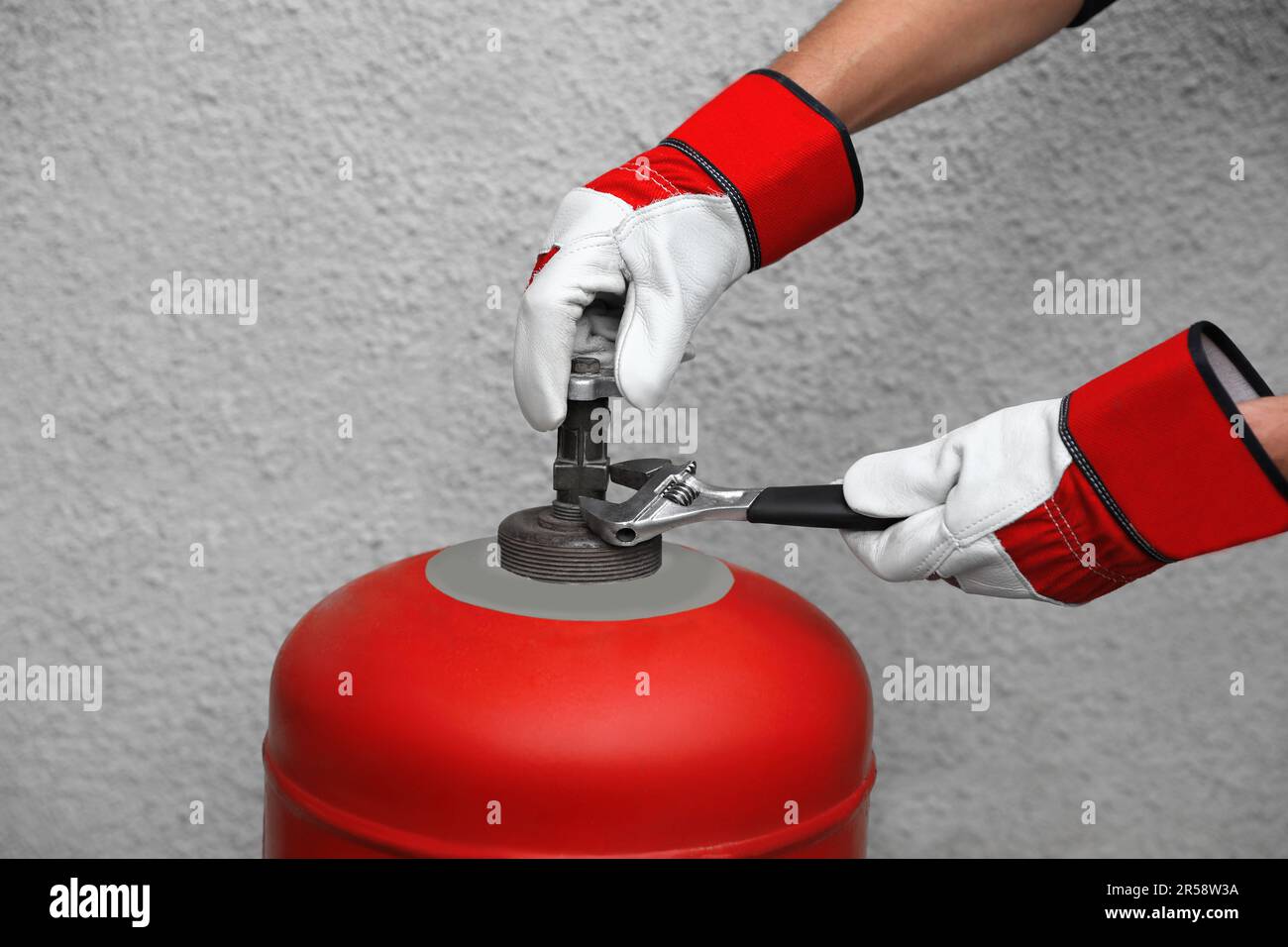 Worker with adjustable wrench opening red gas cylinder near wall ...