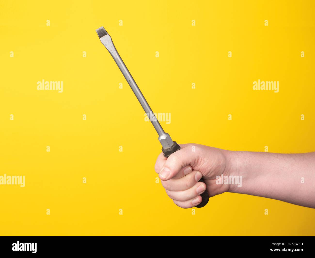 A male hand is holding a very large screwdriver. Yellow background, no ...