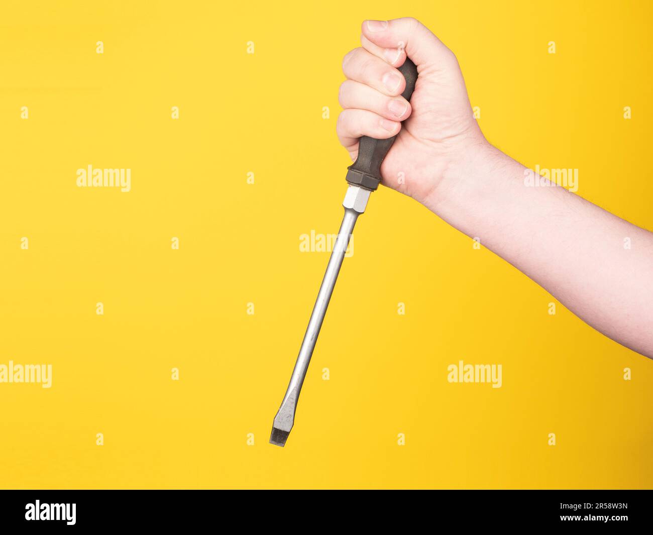 A male hand is holding a very large screwdriver. Yellow background, no ...