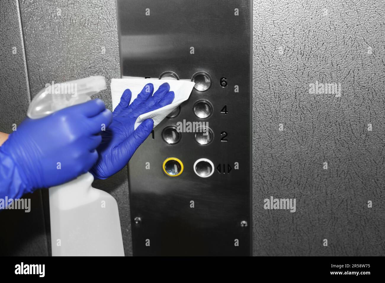Woman wiping buttons of elevator`s panel with detergent and paper ...