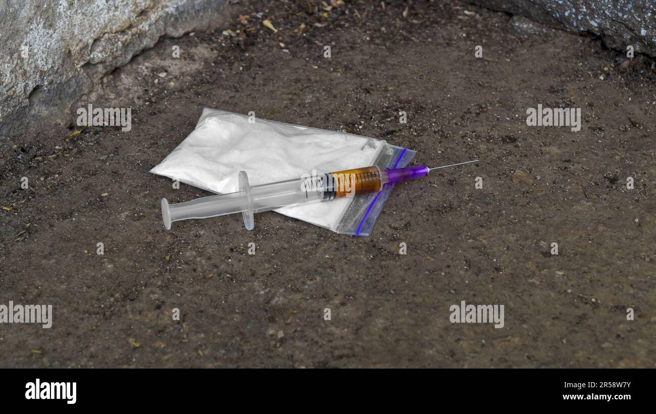 Plastic bag with powder and syringe on asphalt outdoors. Hard drugs ...